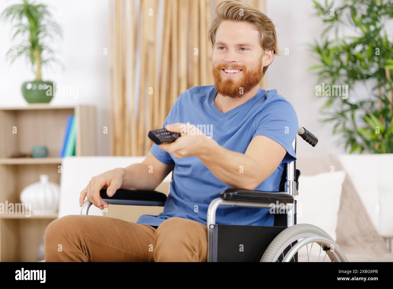 happy young man in wheelchair holding tv remote Stock Photo - Alamy