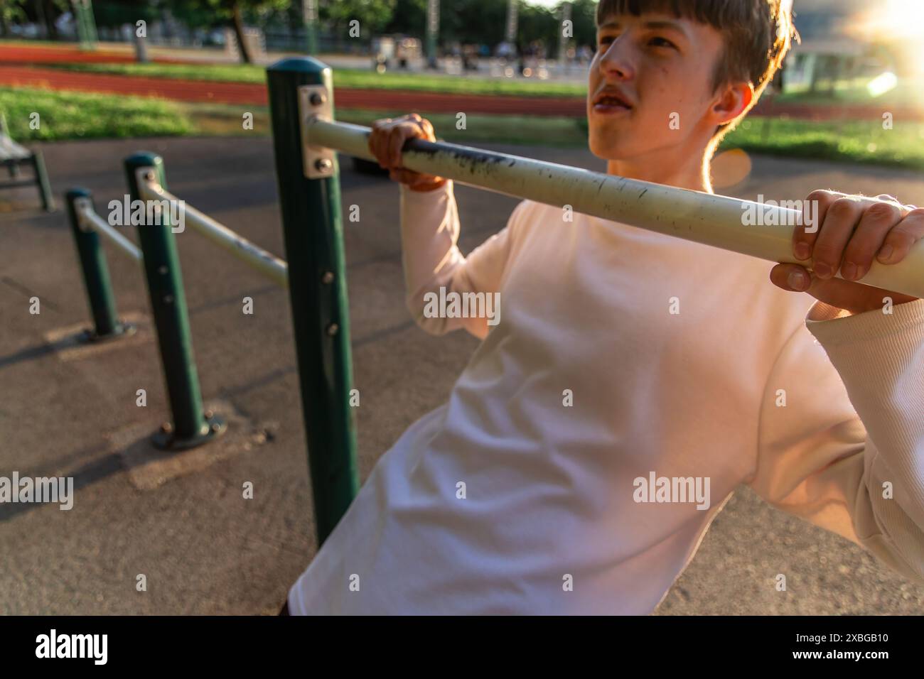 This image shows a teenage boy doing pull ups on a bar in an outdoor ...