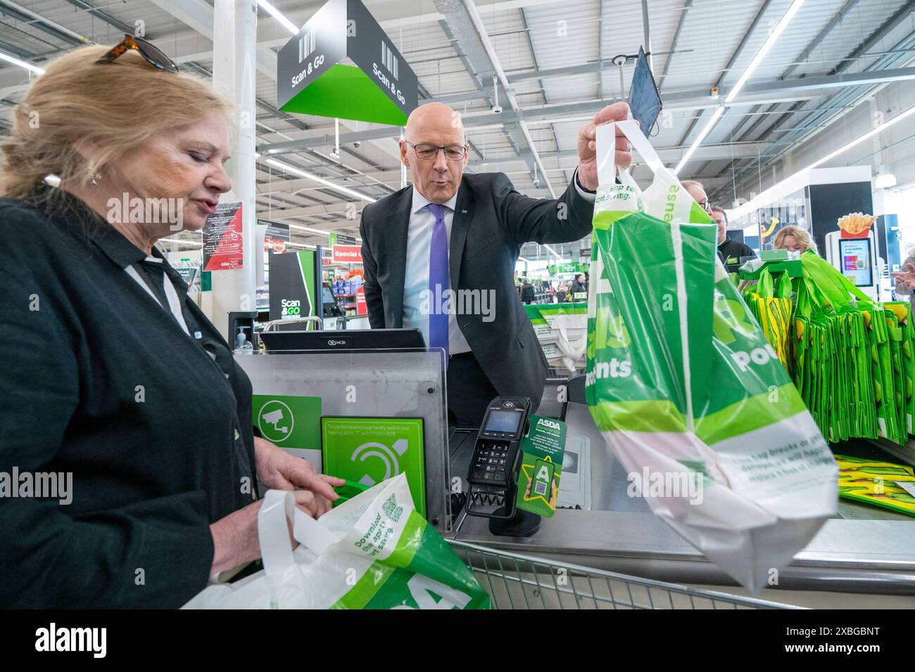 Scottish First Minister John Swinney helps out on the check-out at Asda ...