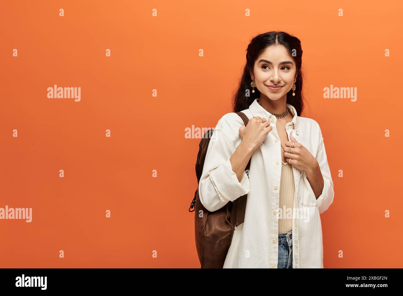 Young indian woman with backpack striking a pose against bright orange ...
