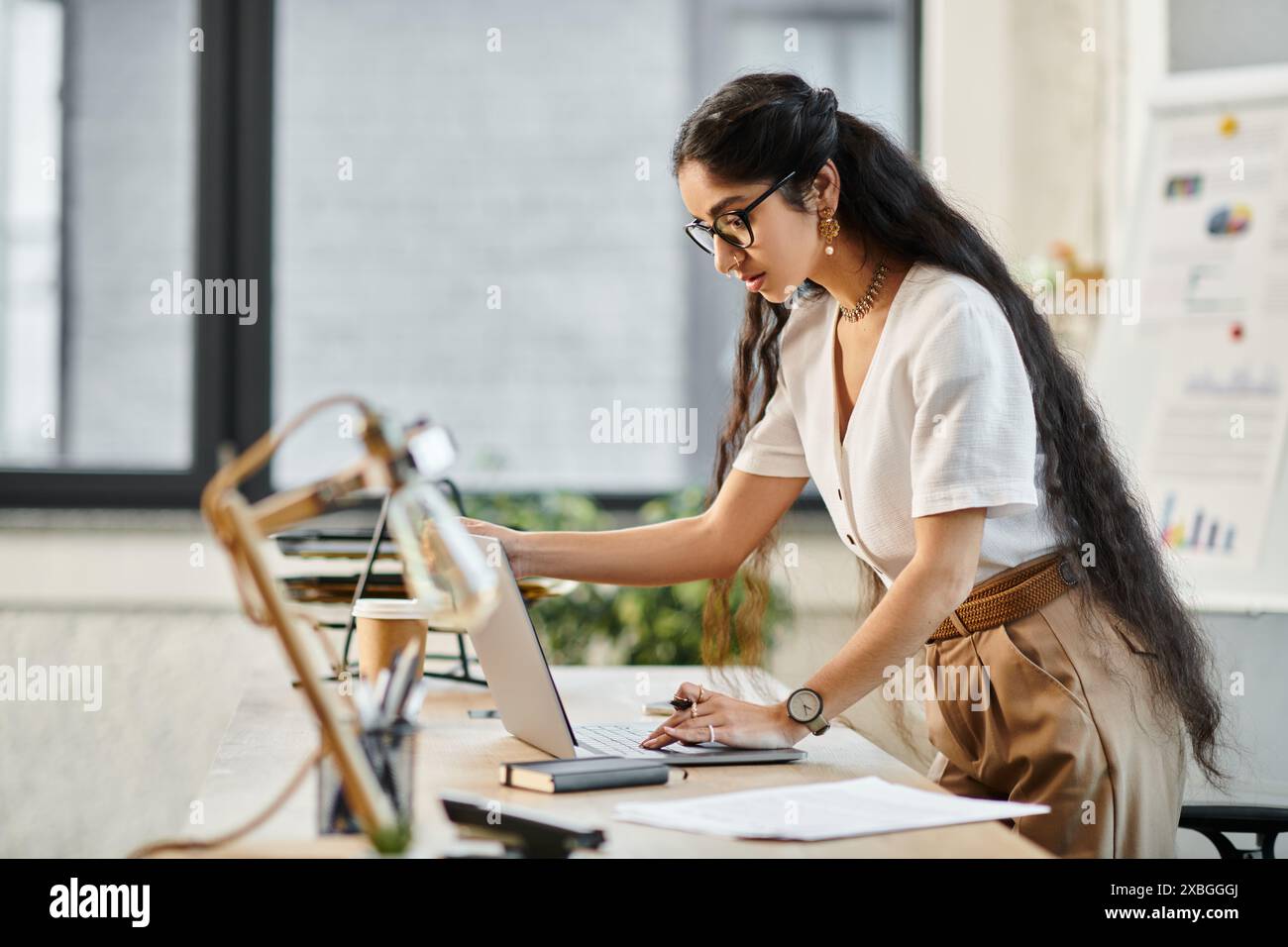 A young indian woman actively working on a laptop in an office setting ...