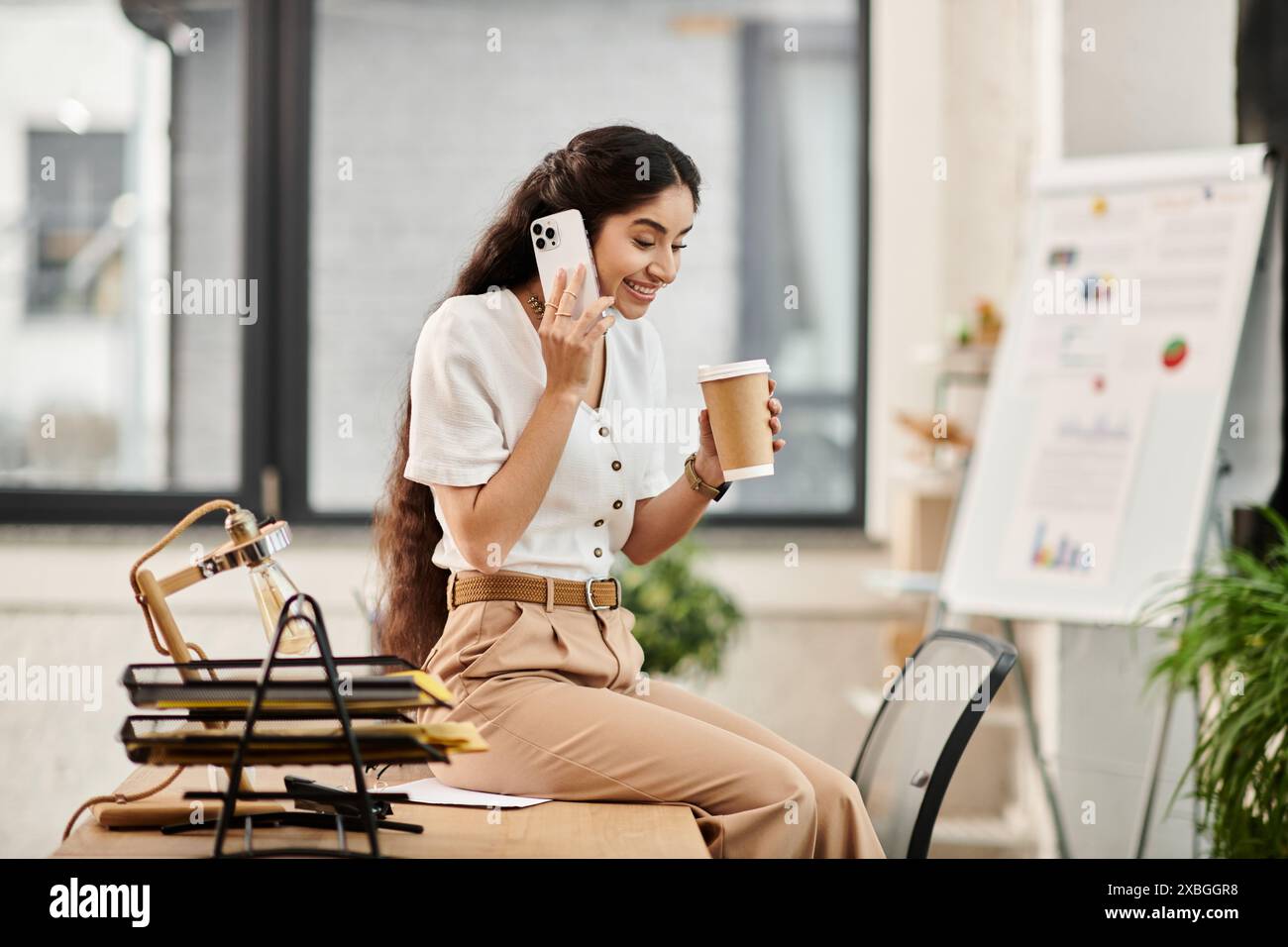 A young indian woman sits at a desk, engrossed in a phone conversation ...