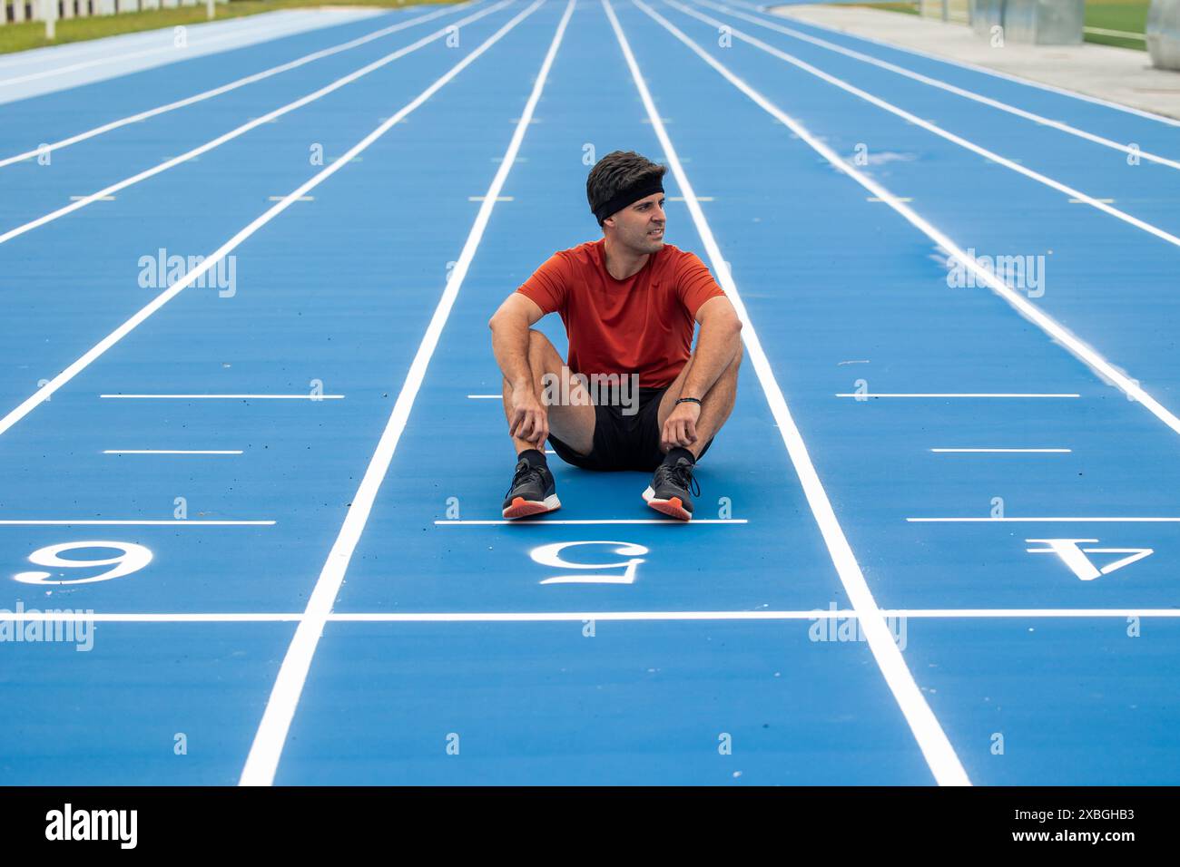 male runner with a headband rests while seated on the finish line of a ...