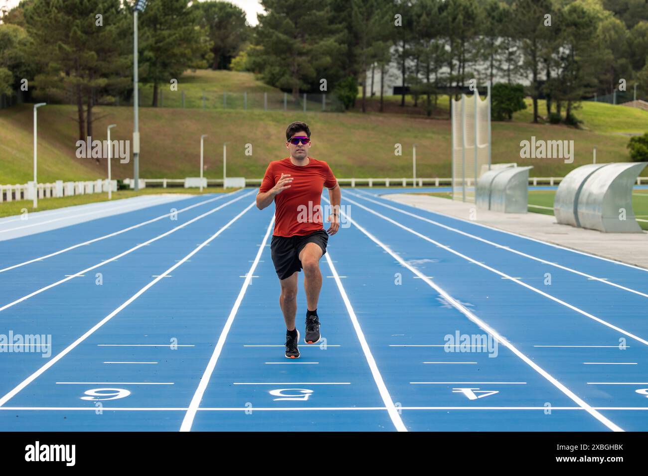 male runner, wearing sunglasses, sprints towards the camera on a blue ...