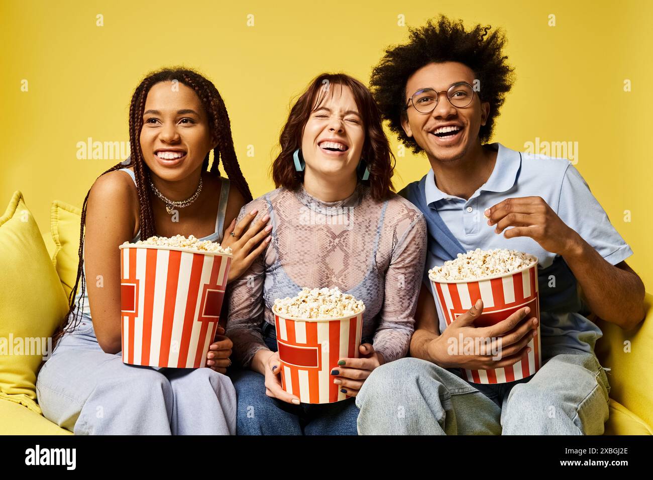 Multicultural young friends sitting on a couch, holding popcorn buckets ...