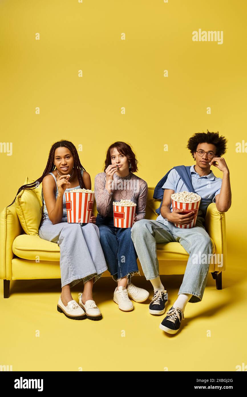 Three young multicultural friends sitting on a couch, munching on ...