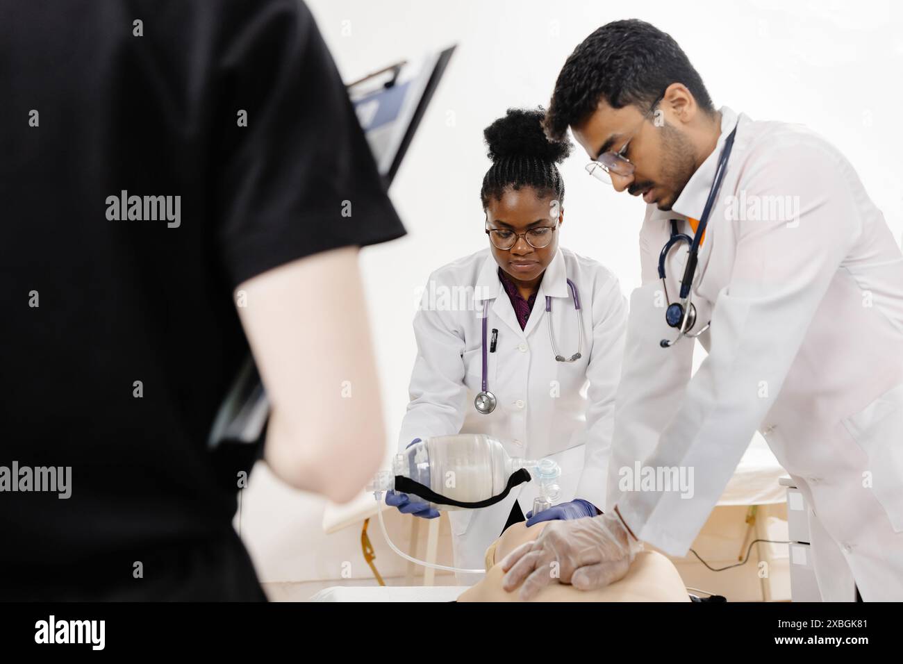 Two medical students in white coats practice CPR on a mannequin while a ...