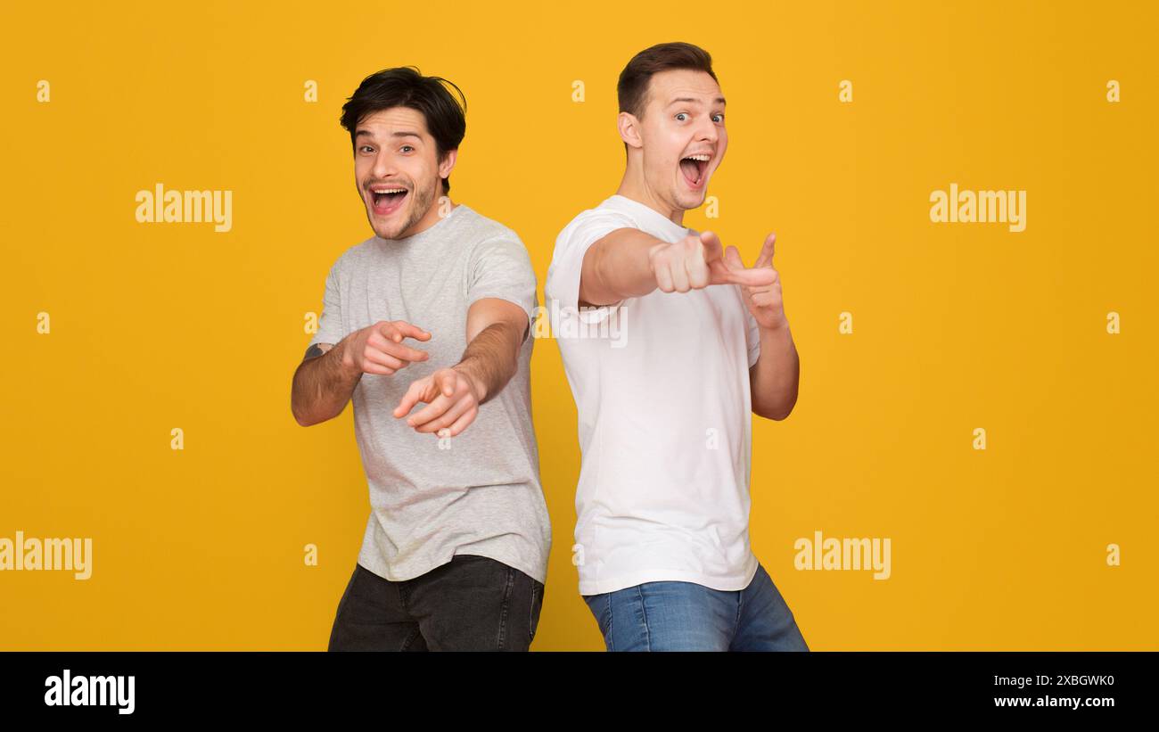 Two men pointing and smiling joyfully on yellow background Stock Photo ...