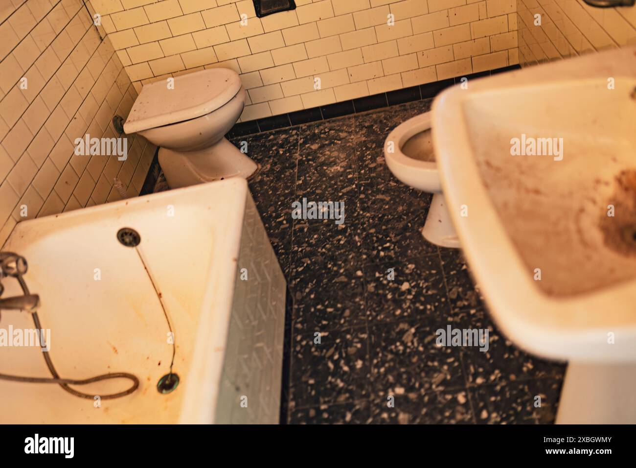 An old, dirty bathroom with a bathtub, toilet, and sink, showing ...