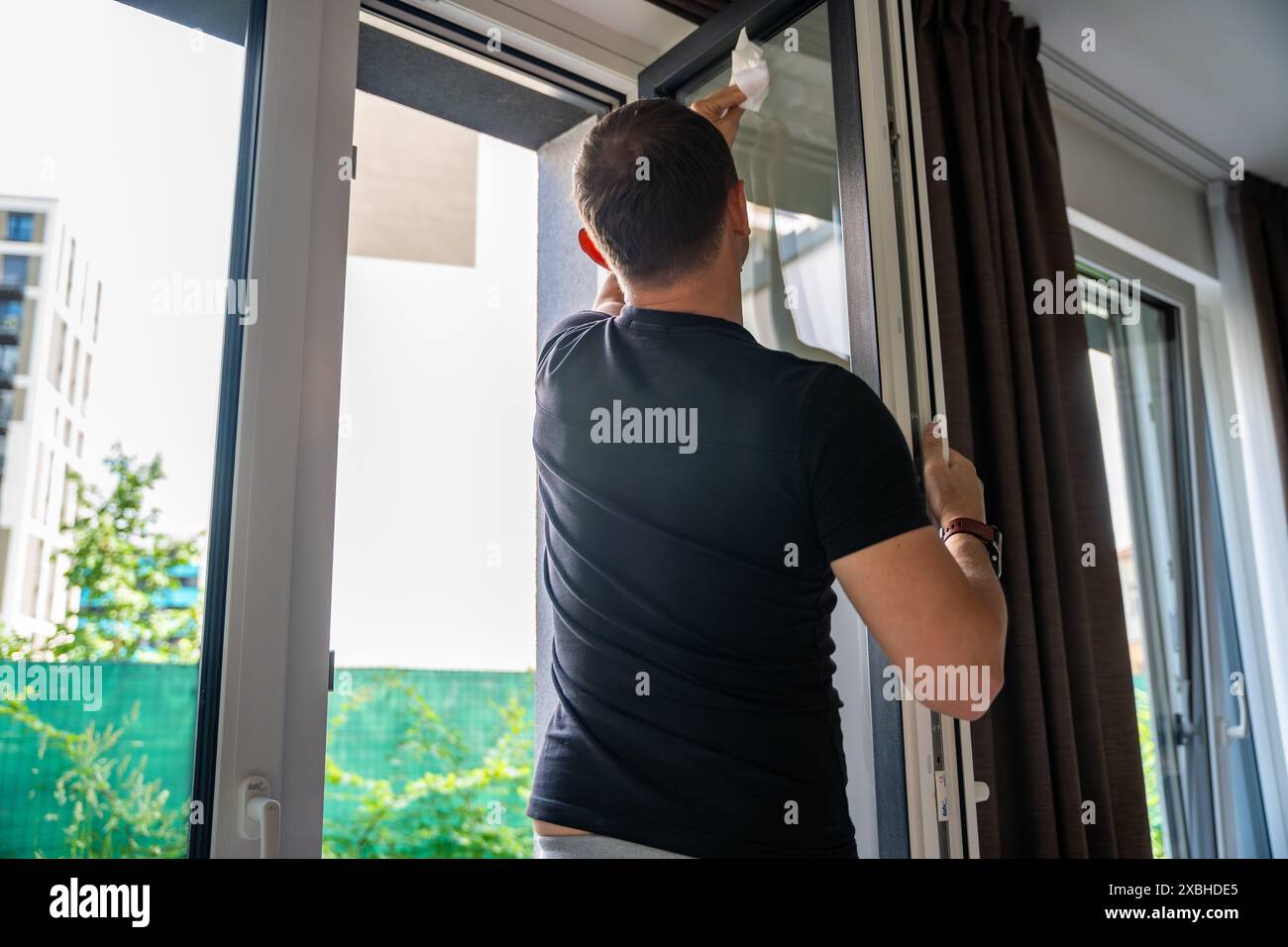 Young man cleans the windows in the house. He splashes detergent, rubs ...