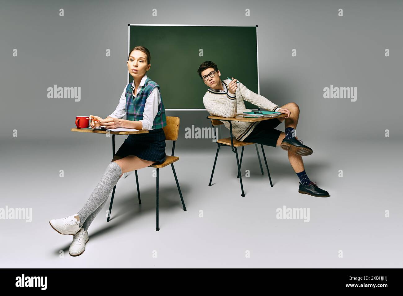 Two stylish students engaged in study at a desk before a green board ...
