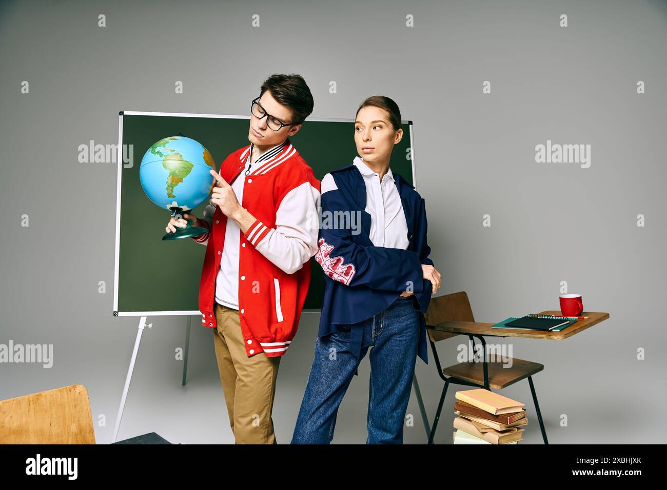 Two students hold a globe, standing in front of a desk in a classroom ...