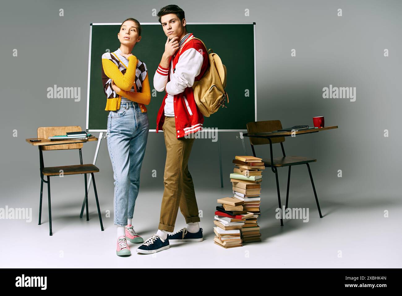 Two young students in casual attire stand in front of a green board in ...