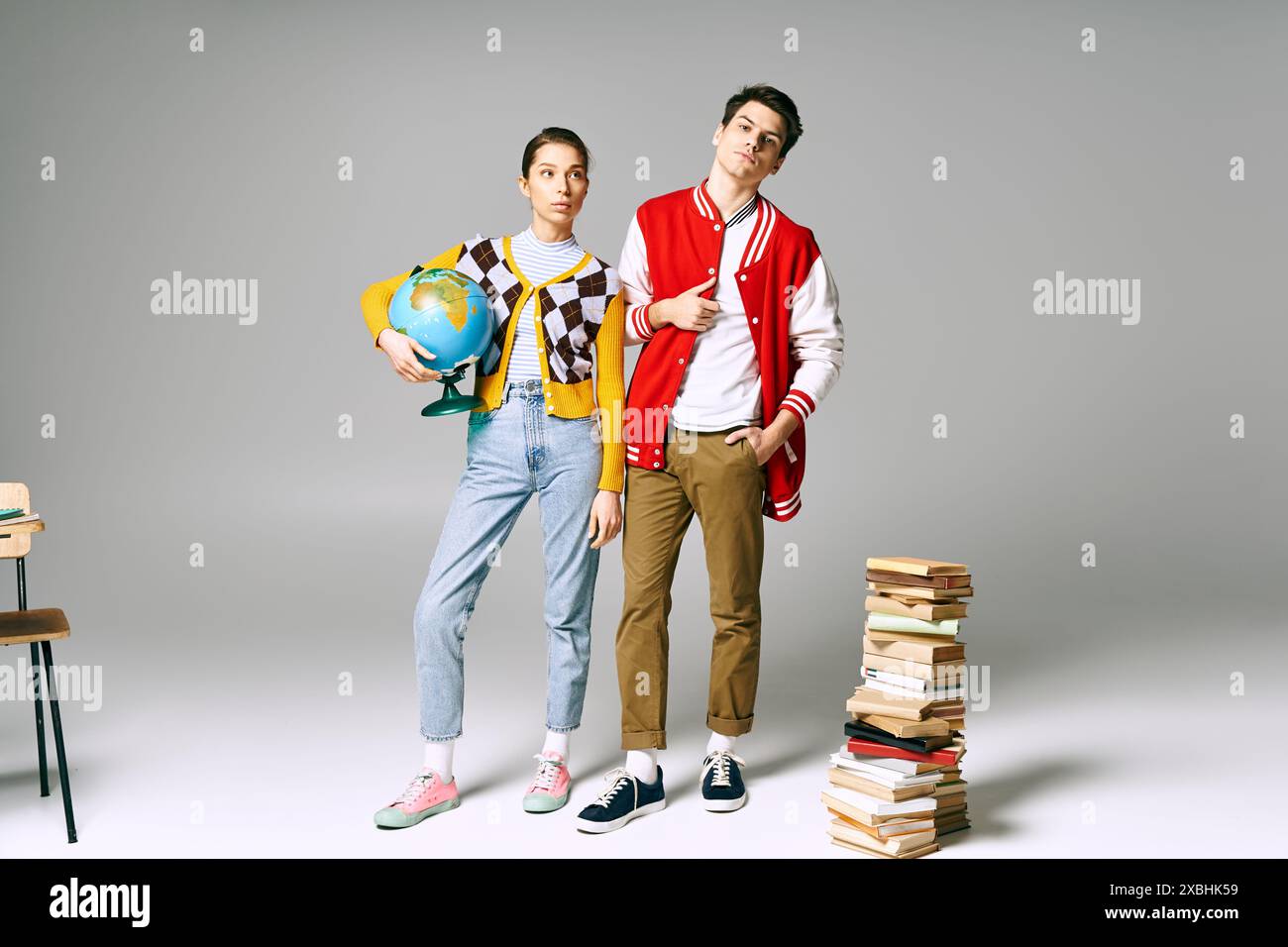 Two young students posing in front of a tall stack of books in a ...