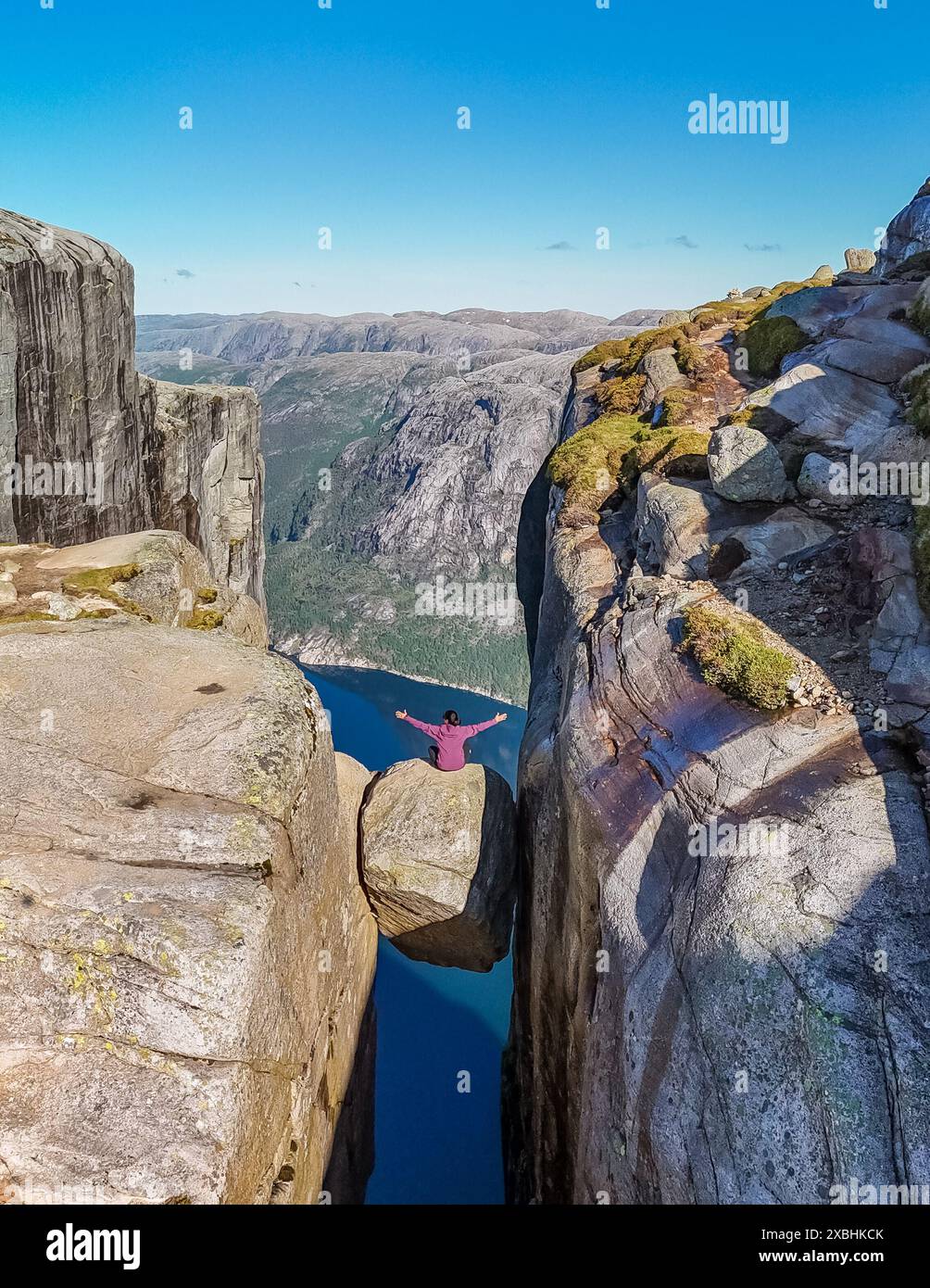 A lone hiker sits on a boulder overlooking a dramatic cliff face in ...