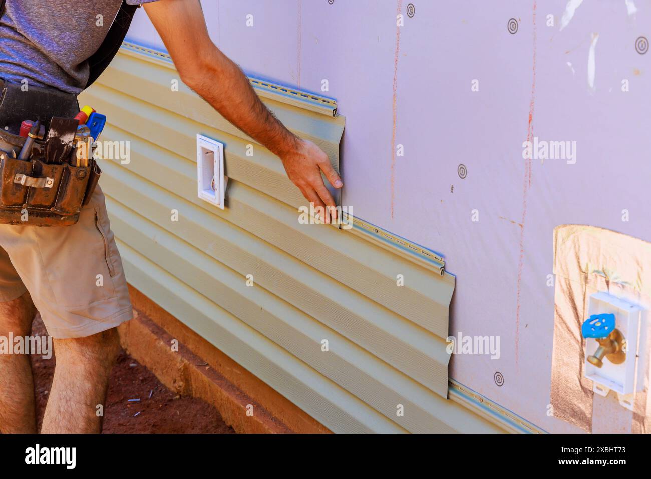 An employee installs vinyl plastic siding panels on wall facade of new ...