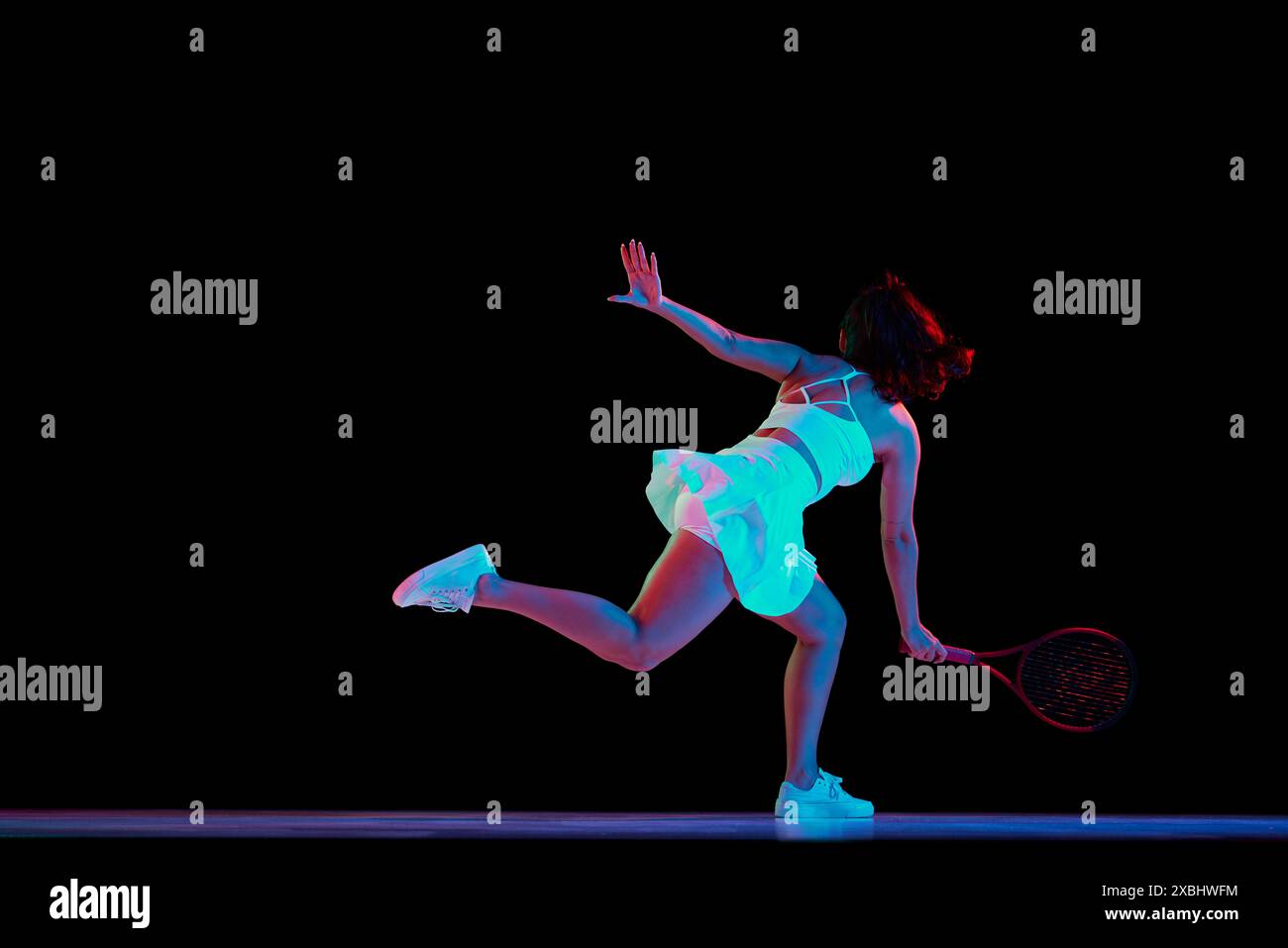 Back view of female athlete in white sport outfit swings her racquet in ...