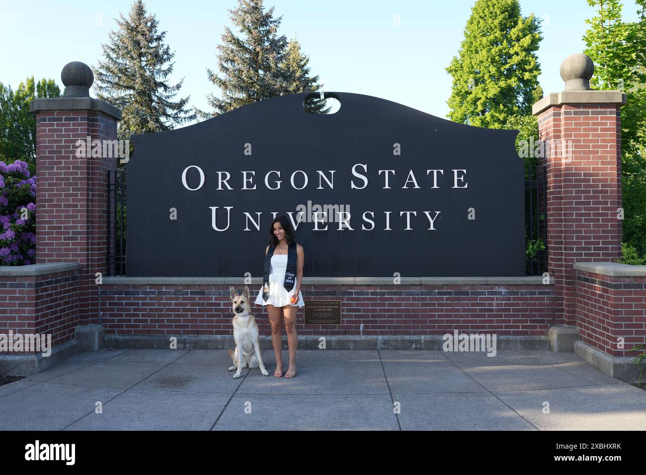 A female student poses with graduation stole and dog at sign at the ...
