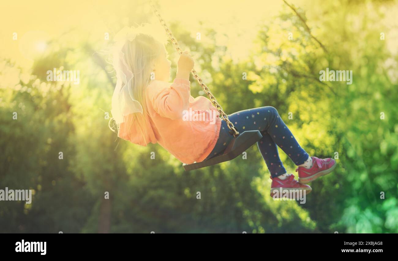 happy preschool girl swings high on summer day, blurred child figure in ...