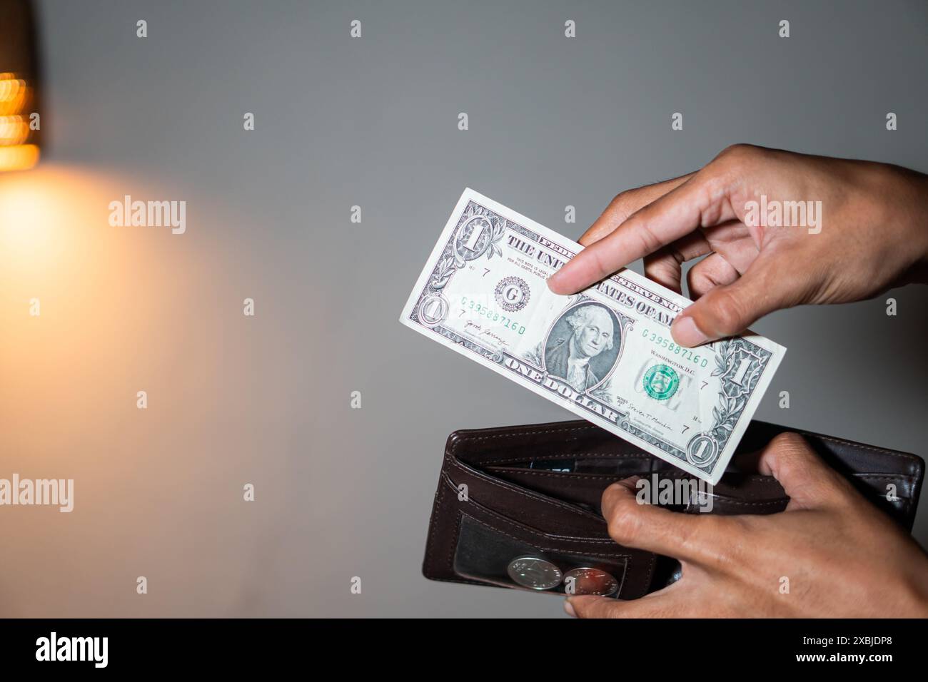 A person holding a one-dollar bill and a brown wallet with coins ...