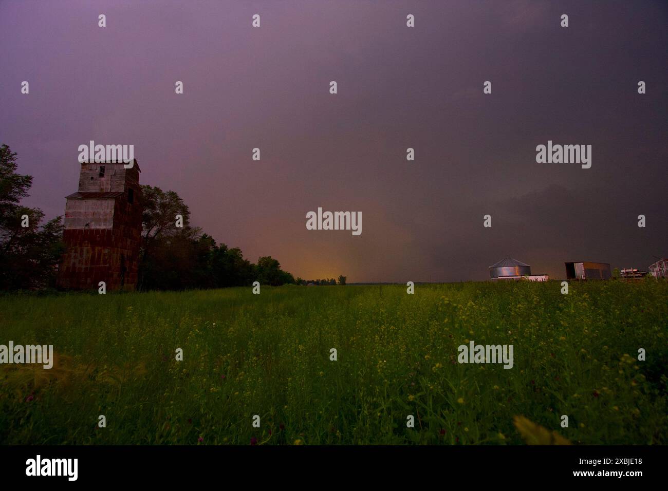 Old grain mill in a lush meadow, illuminated by lightning at night ...