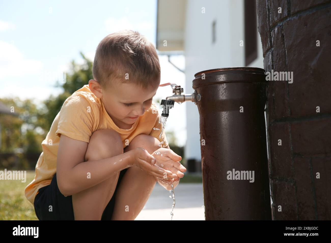 Water scarcity. Cute little boy drawing water with hands from tap ...