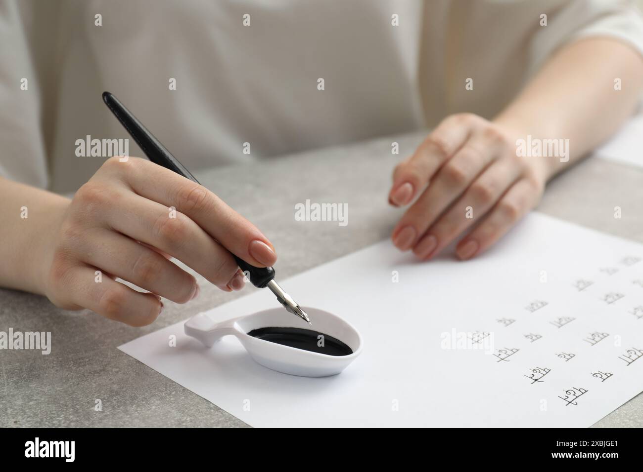 Calligraphy. Woman dipping fountain pen into inkwell at grey table ...