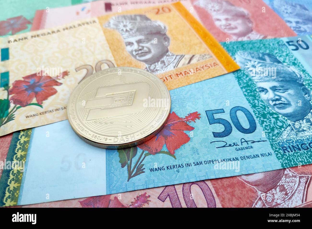 Close-up on a golden Dash coin on top of a stack of Malaysian Ringgit ...