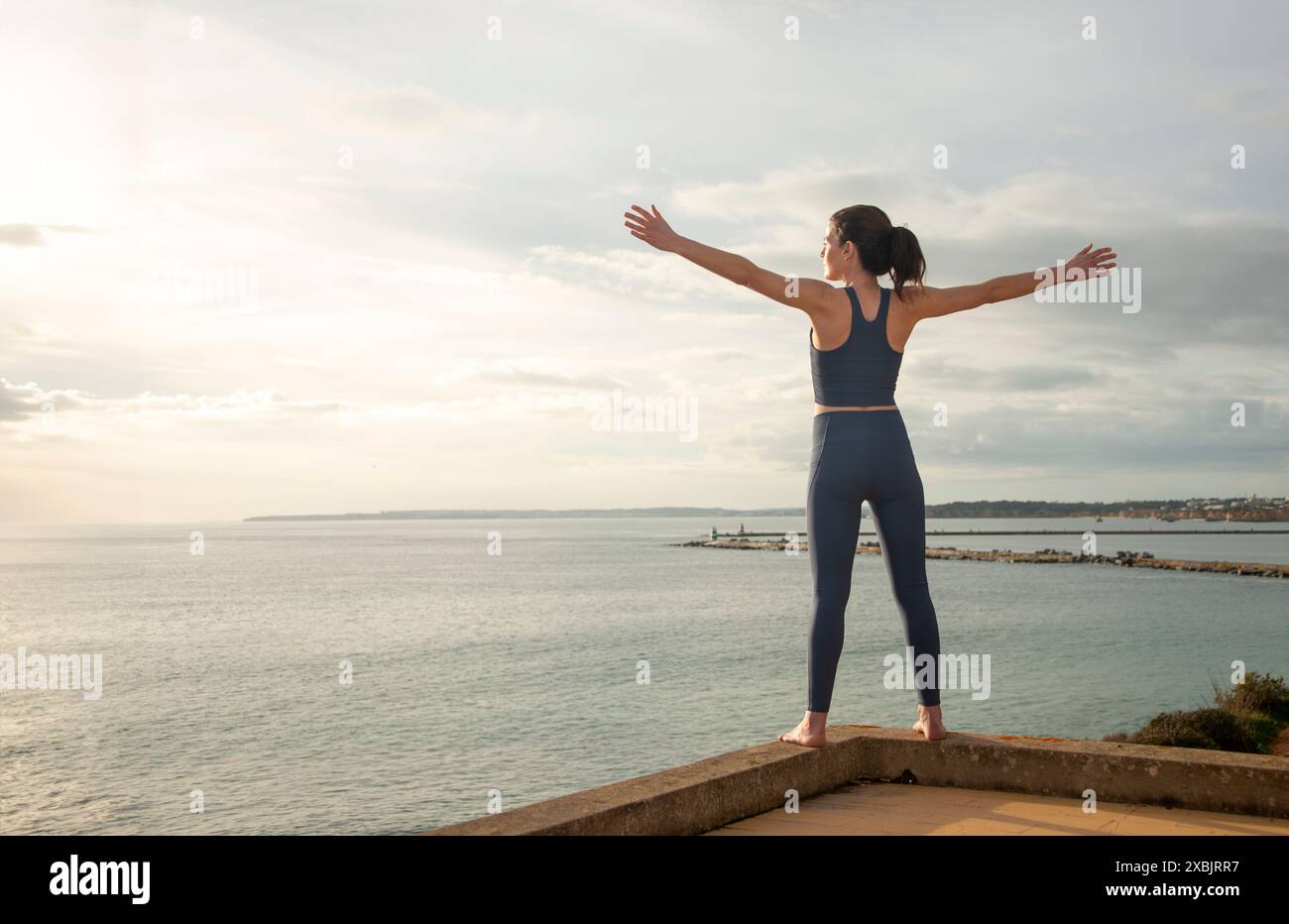 rear view of a sporty woman with her arms raised in celebration by the ...