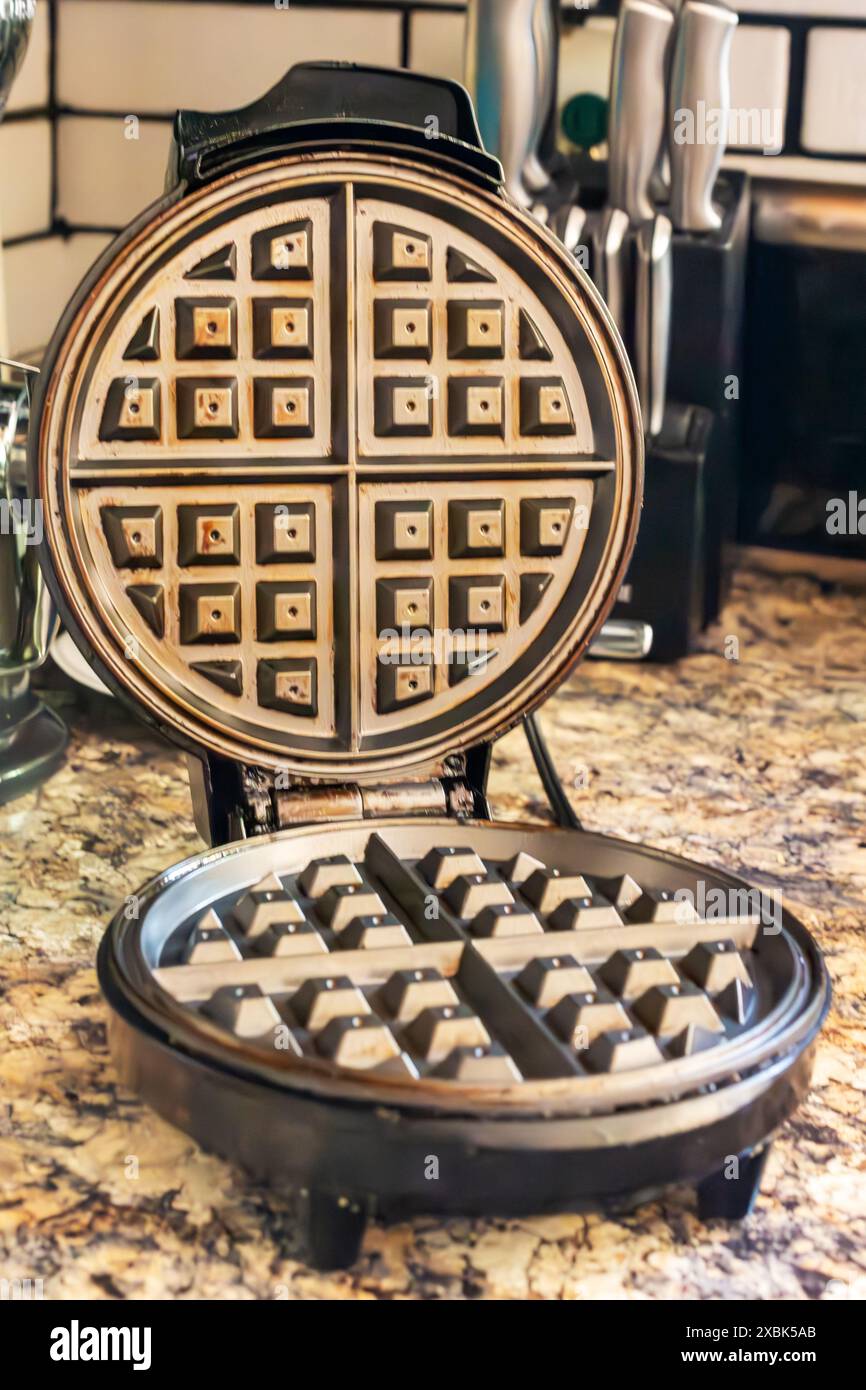 A well-loved electric waffle iron with its lid open on a kitchen ...