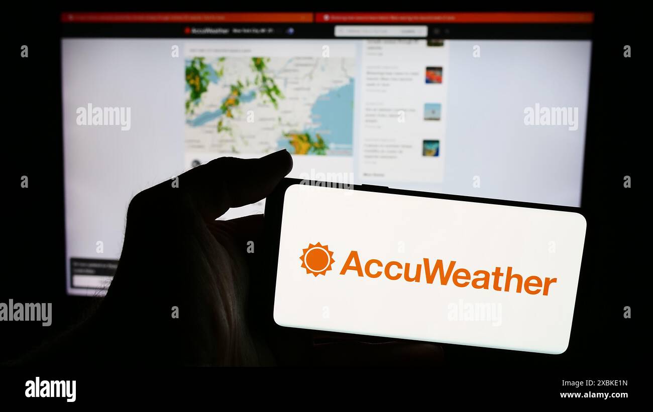 Person holding mobile phone with logo of American weather forecasting ...