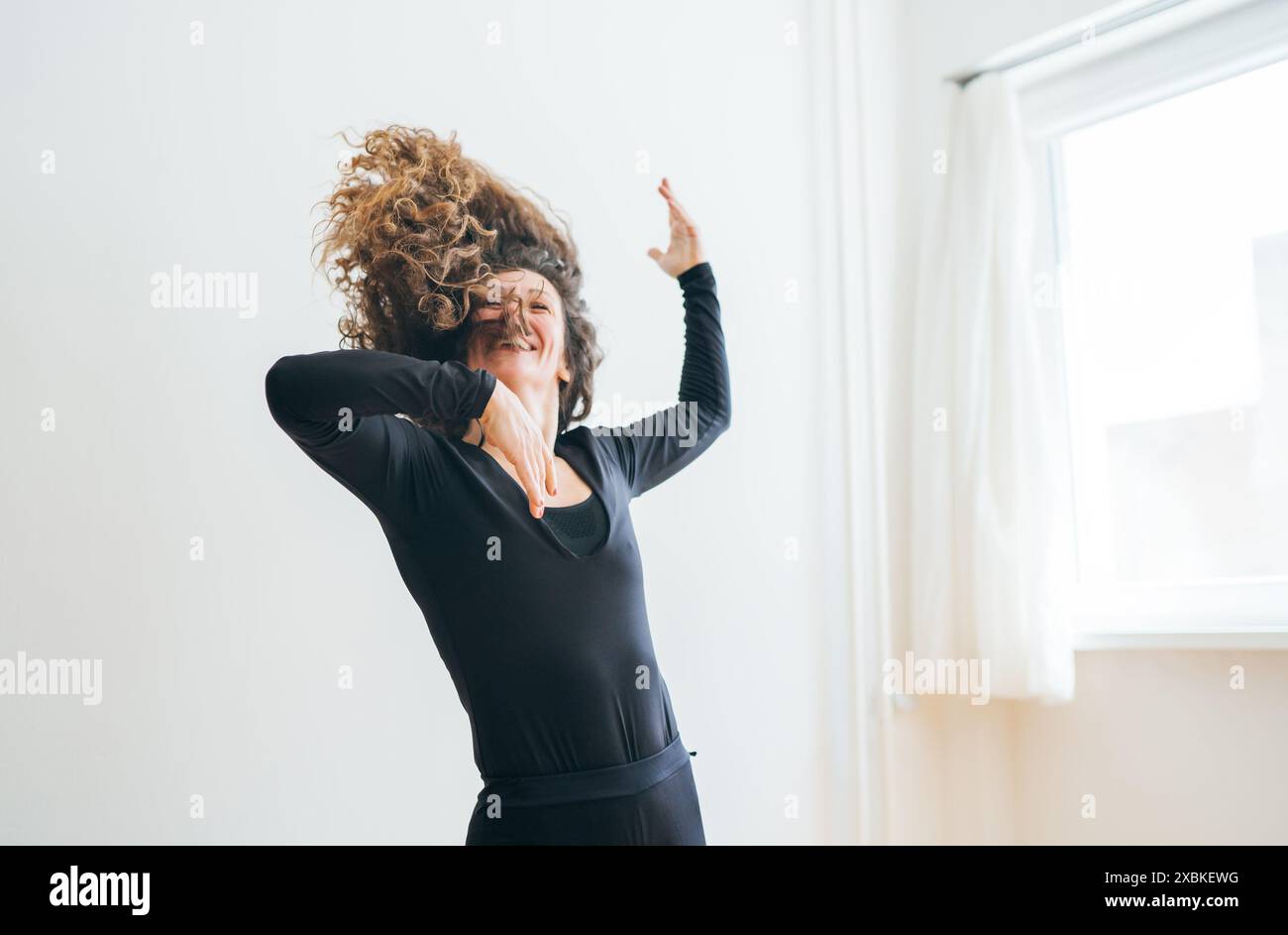 woman in black outfit laughs joyfully while dancing curly hair ...