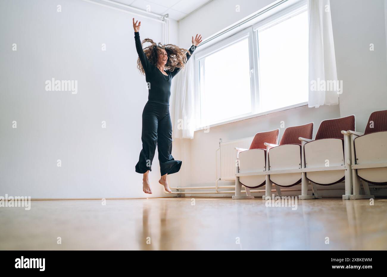 Woman in a black outfit gracefully jumping in a well-lit room, her ...