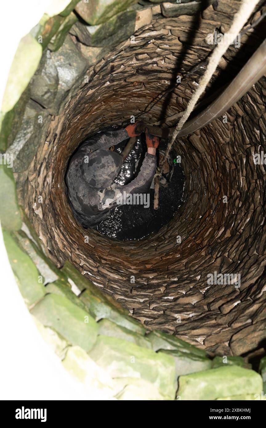 A man in the middle of a well cleans the bottom of dirt and accumulated ...