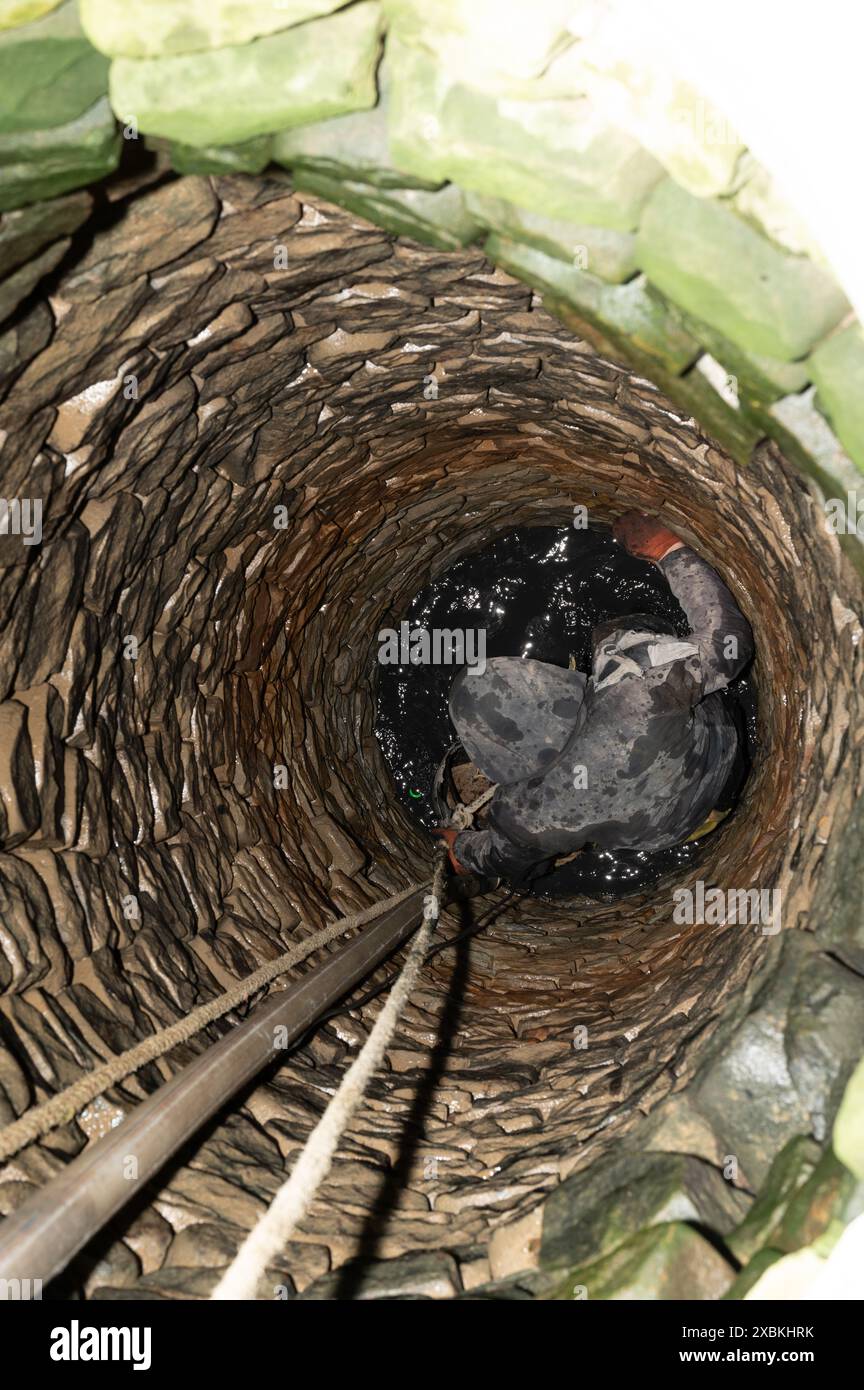 A man in the middle of a well cleans the bottom of dirt and accumulated ...