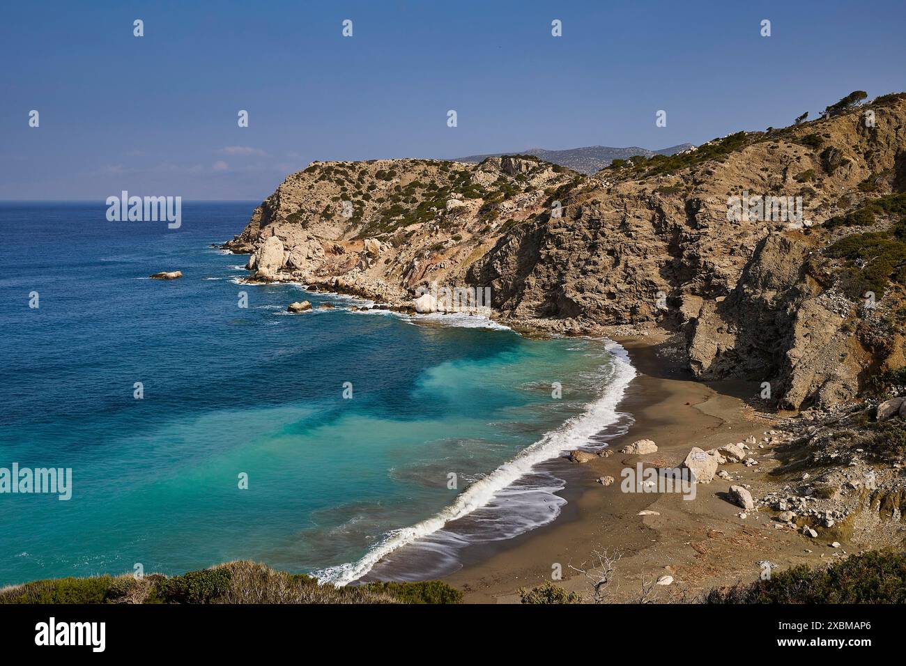 Coastal strip with steep rocks on the beach and blue water under a blue ...