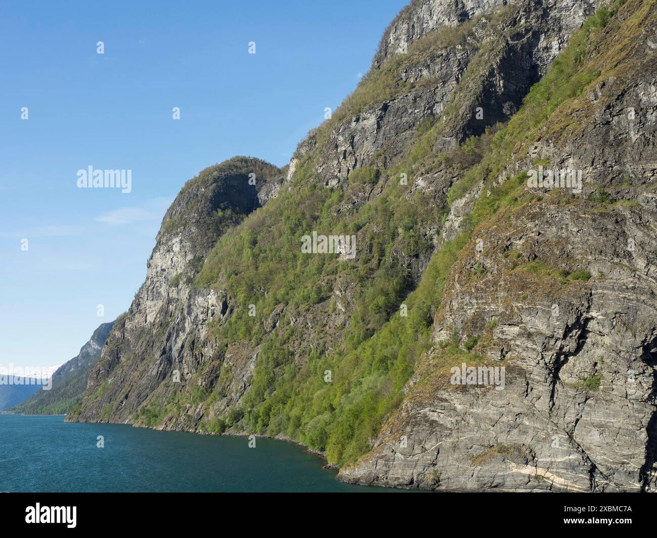 High mountains with steep rock faces and green trees rising next to the ...