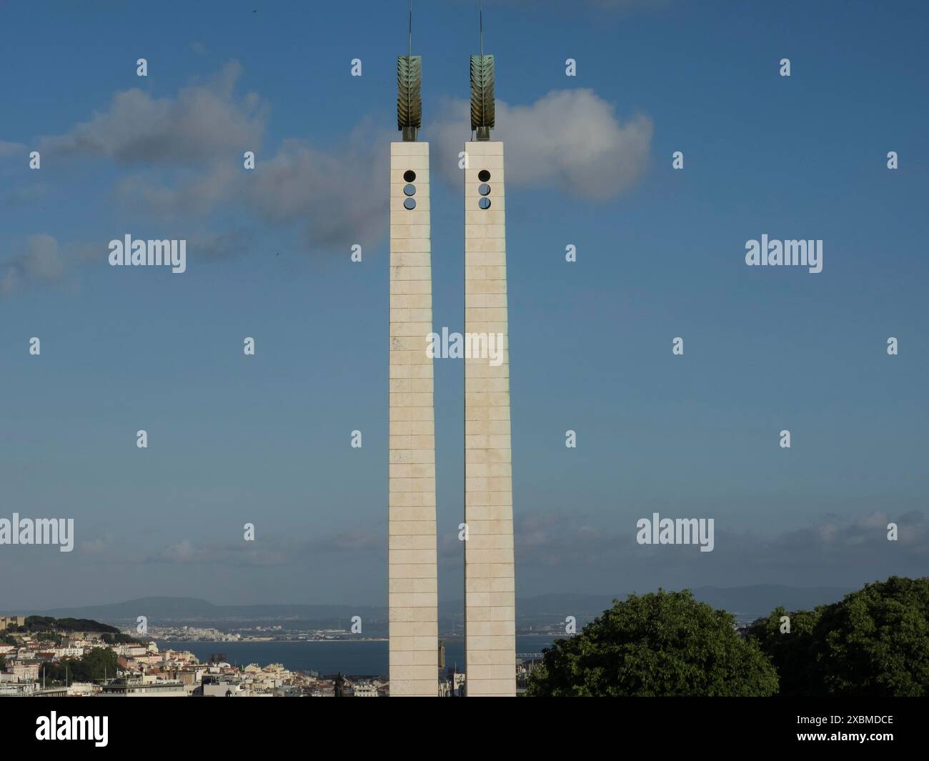 Two identical towers rise into the sky above a city with many trees ...