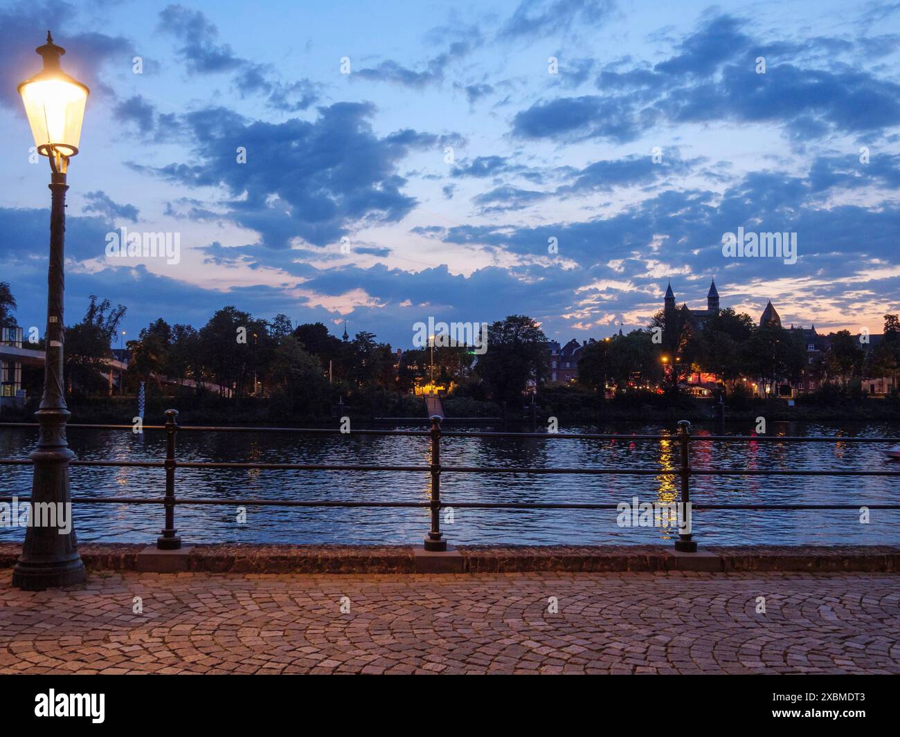 Quiet riverside scene at dusk with street lamp and clouds in the sky ...