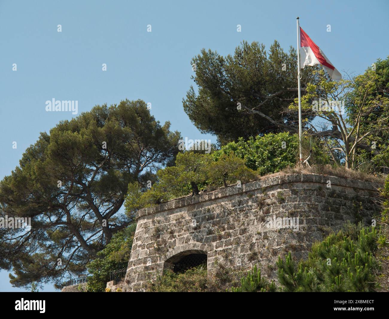An old stone wall with a red and white flag and surrounded by trees and ...