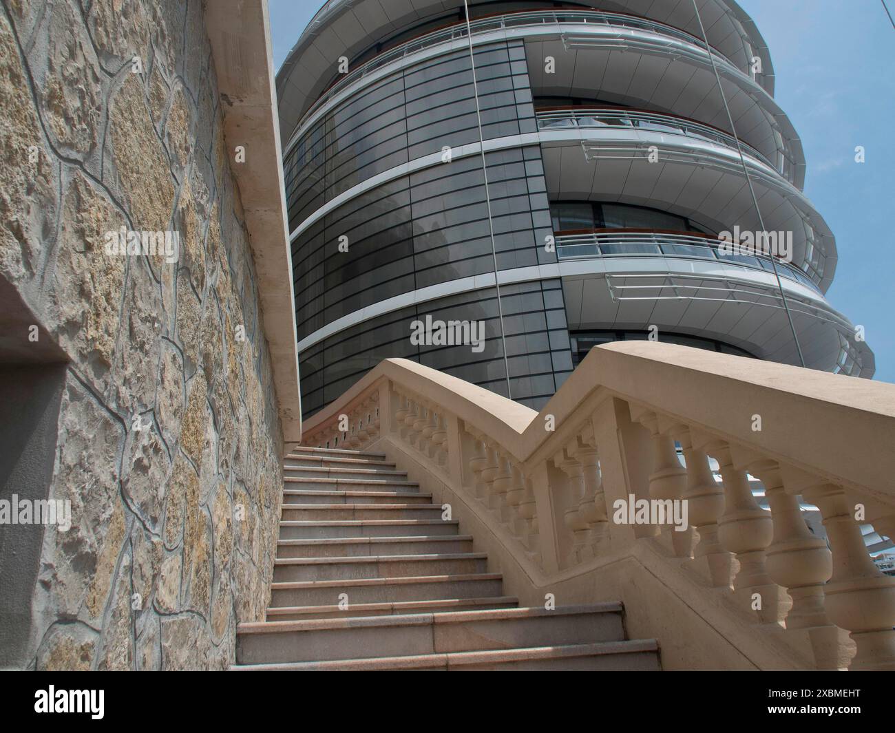 A modern structure with a curved glass building and a stone staircase ...