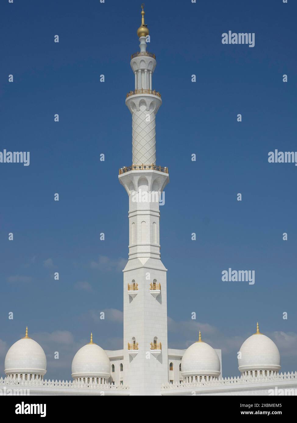 Tall minaret with elaborate details, flanked by domes under a blue sky ...