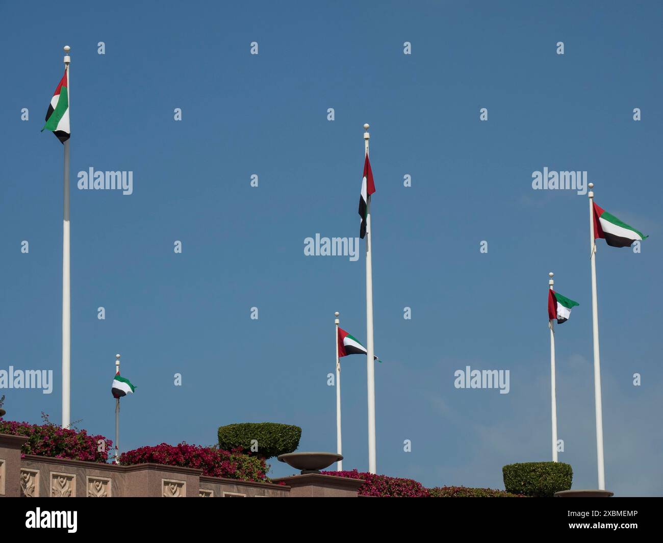 Several national flags on high flagpoles in front of a blue sky, abu ...