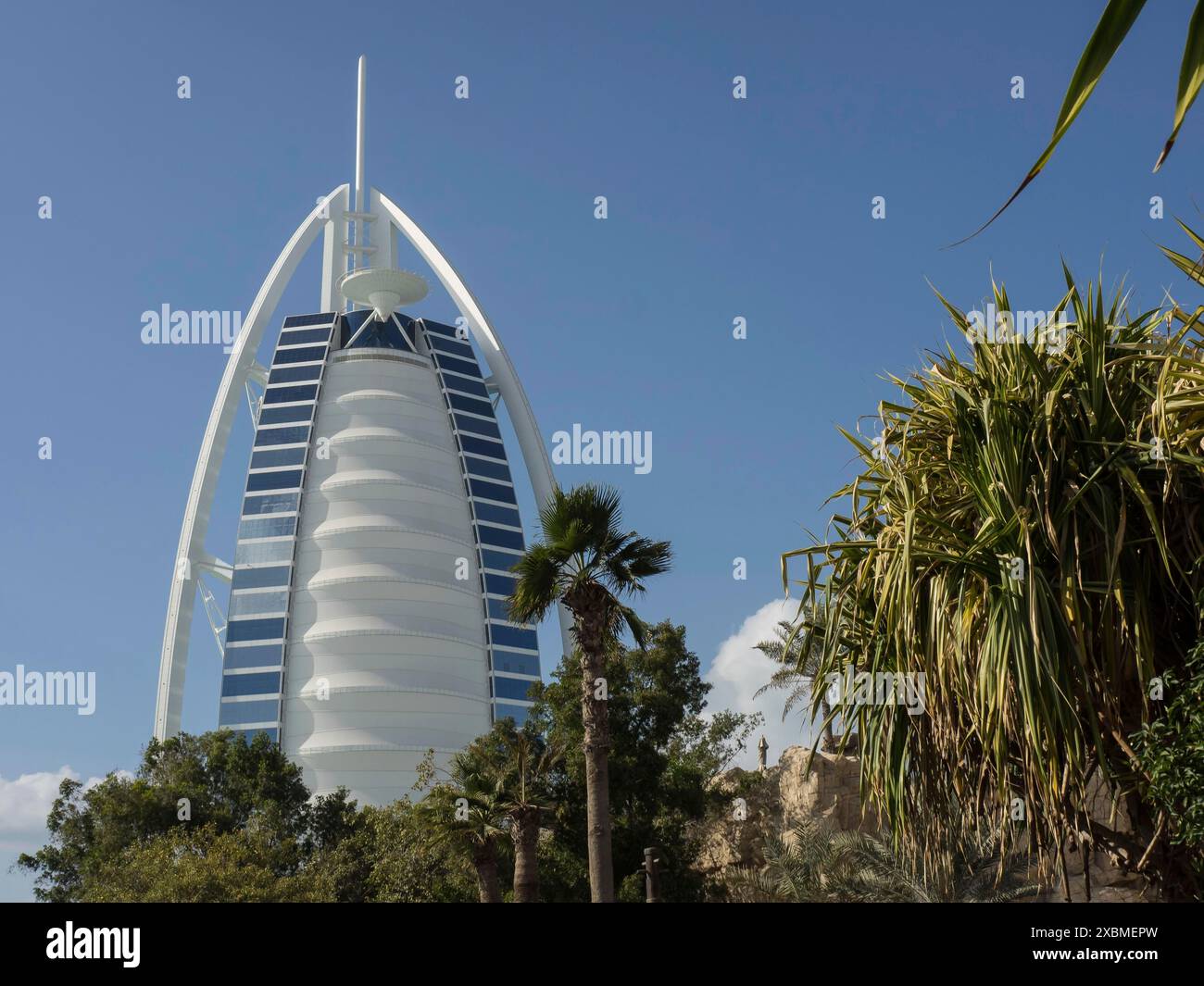 A view of the modern and luxurious Burj Al Arab building surrounded by palm trees under a blue ...