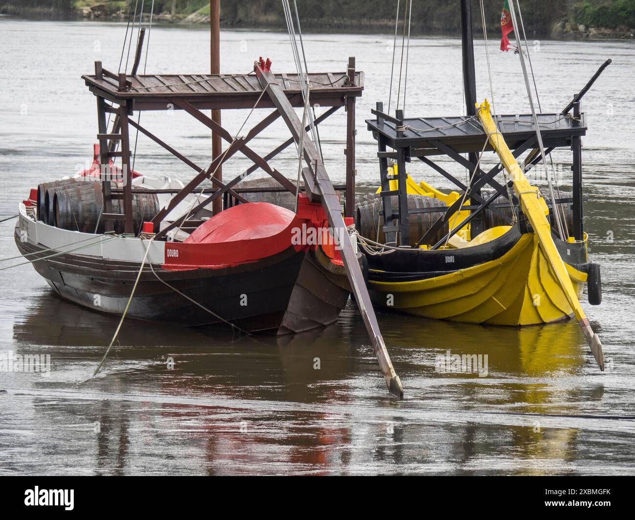 Two boats with wooden structures and large port wine barrels on a river ...