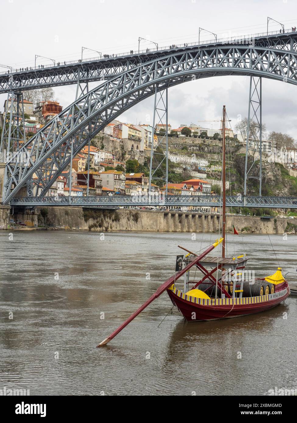 A traditional boat with wine barrels floats under a large metal bridge ...