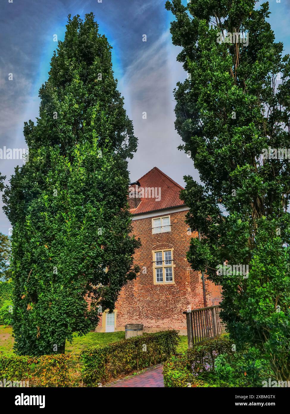 Red brick building with many windows, flanked by tall, green trees and ...