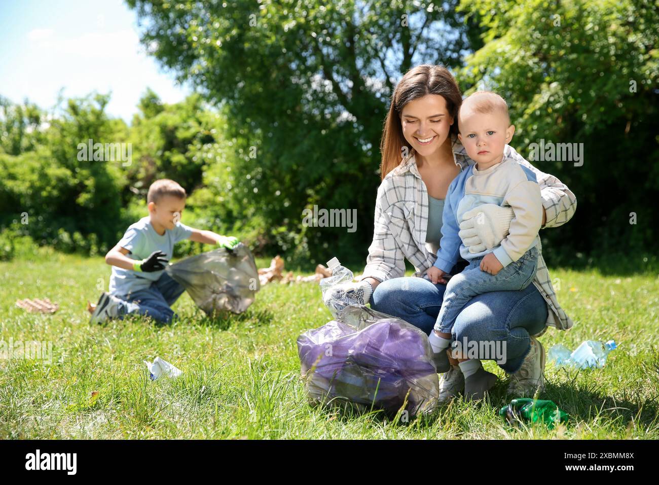 Mother and her children with plastic bags collecting garbage in park ...