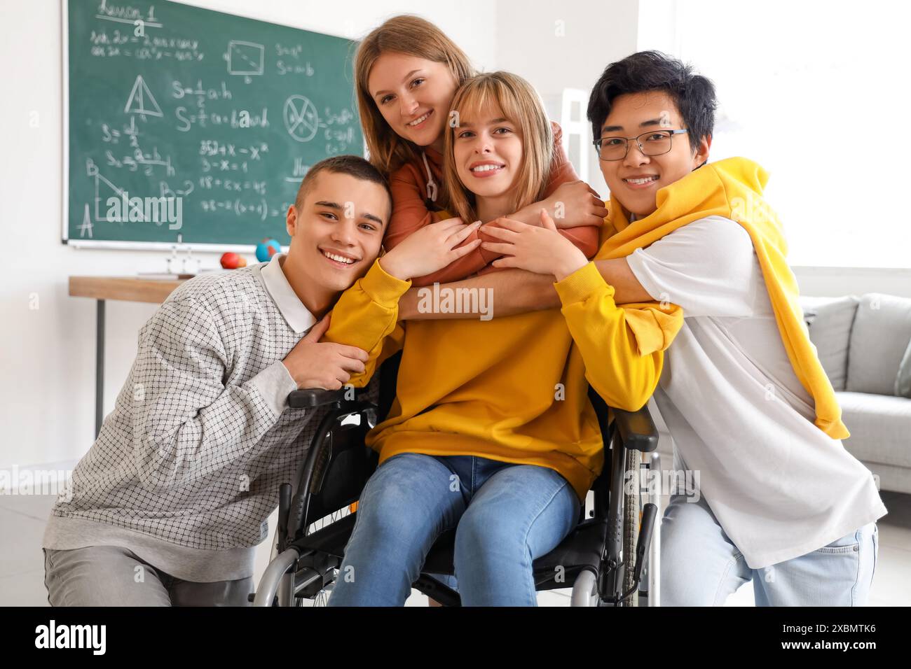 Group of teenage students with girl in wheelchair hugging at school ...