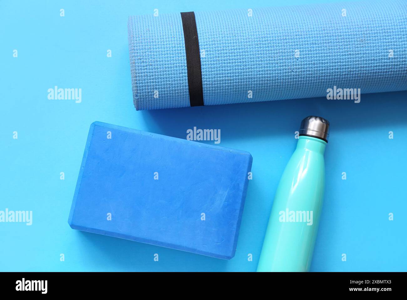 Yoga mat, foam exercise block and bottle of water on blue background ...